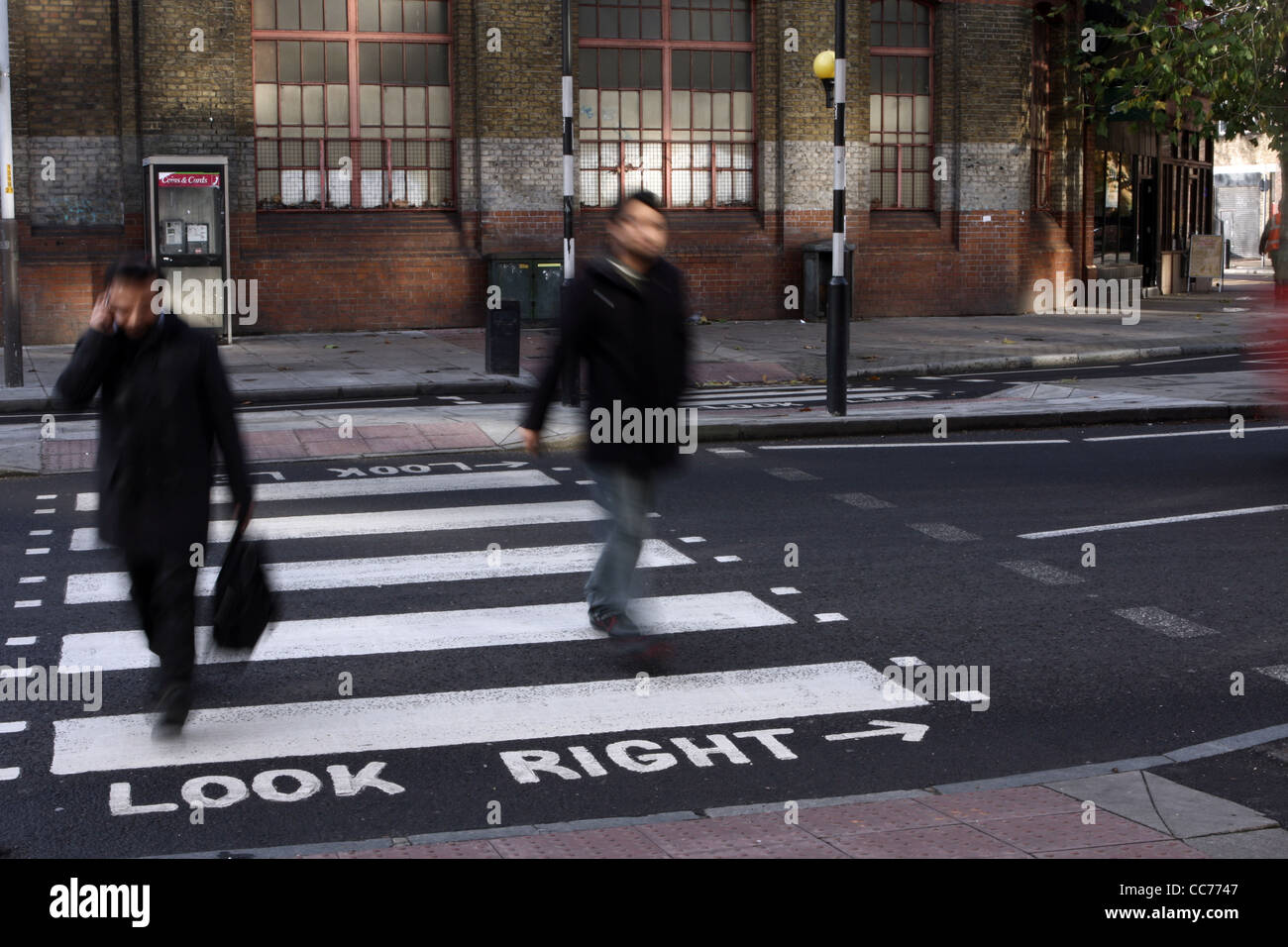 two men walk across a zebra crossing in London - one holding a mobile ...