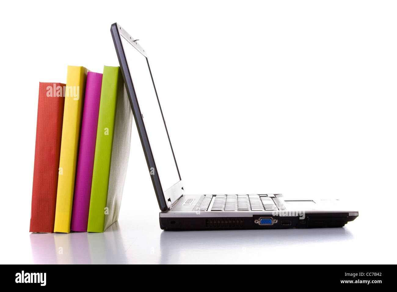 a laptop next to a stack of colorful books Stock Photo - Alamy