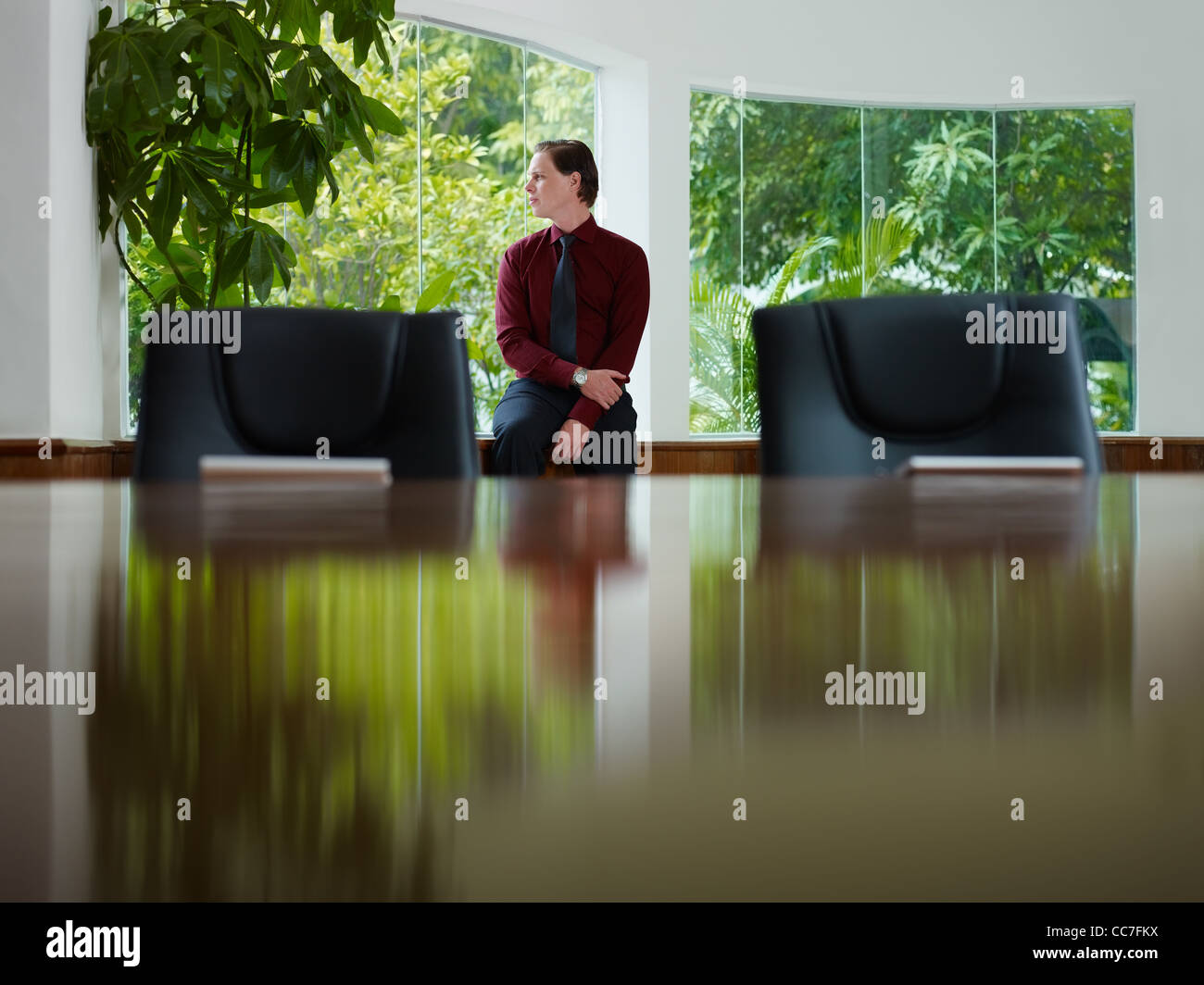 Pensive young business man looking out of the window in meeting room ...