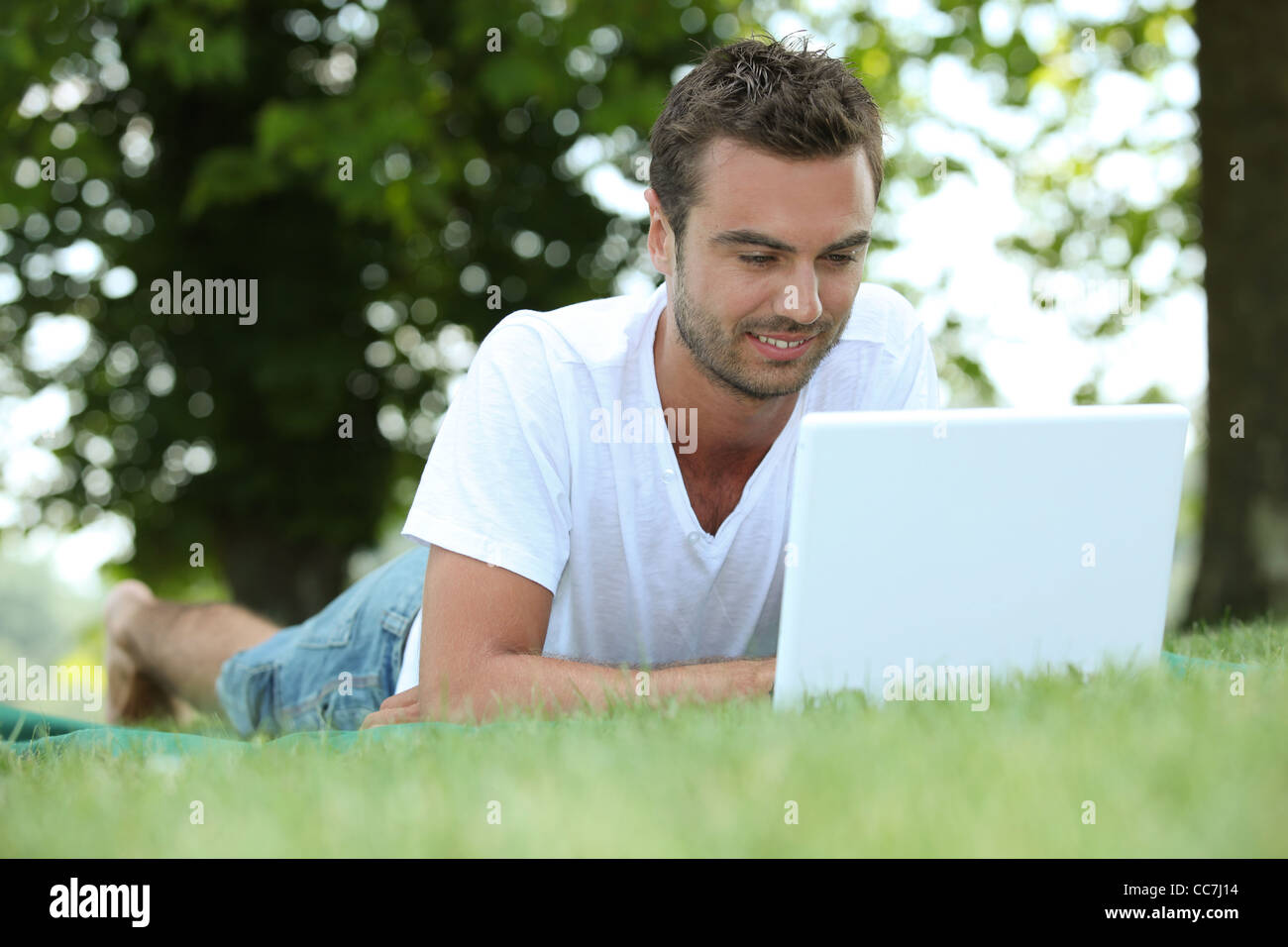Man laid in field with laptop computer Stock Photo - Alamy