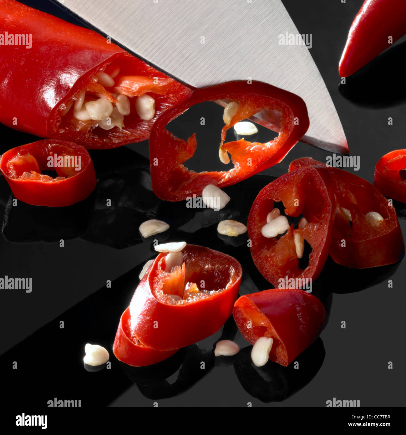 detail of cutting red chili slices with big blade in dark reflective ...
