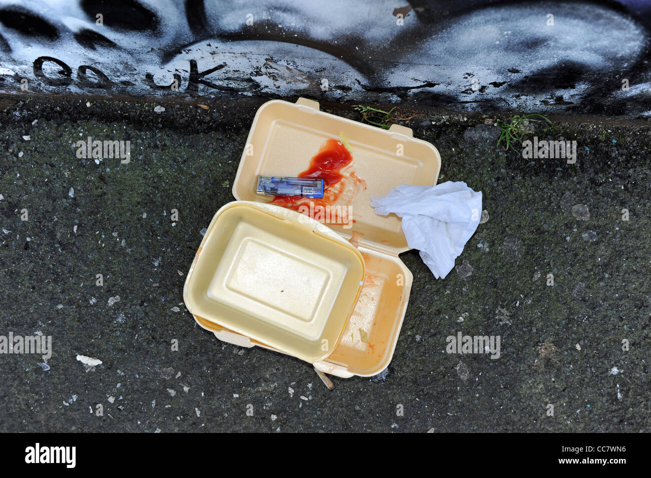 Fast food container thrown away on pavement with tomato sauce and paper ...