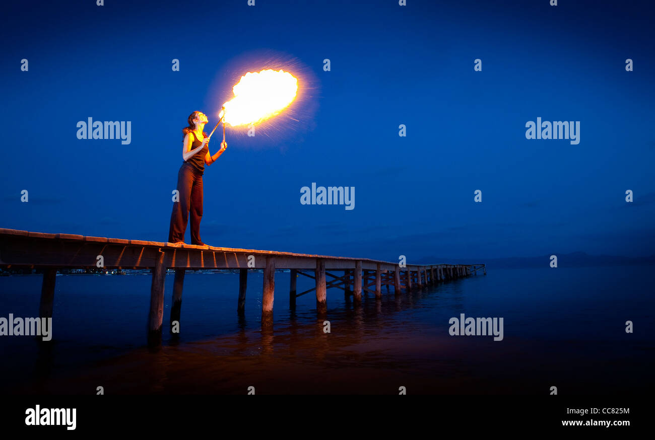 Female fire eater performing on the beach pier, Alcudia at dusk ...