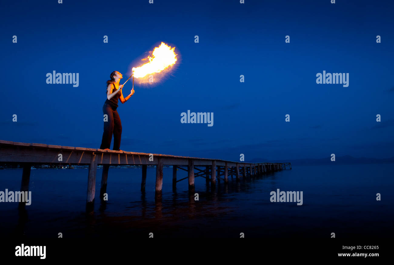 Female fire eater performing on the beach pier, Alcudia at dusk ...
