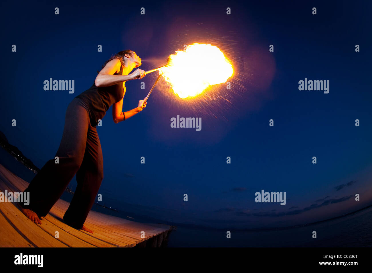Female fire eater performing on the beach pier, Alcudia at dusk ...