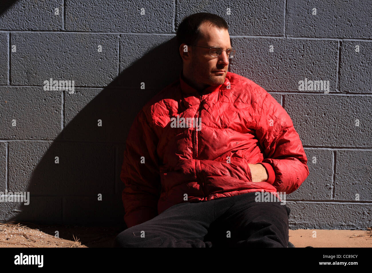 homeless man in red down jacket napping against a wall Stock Photo - Alamy