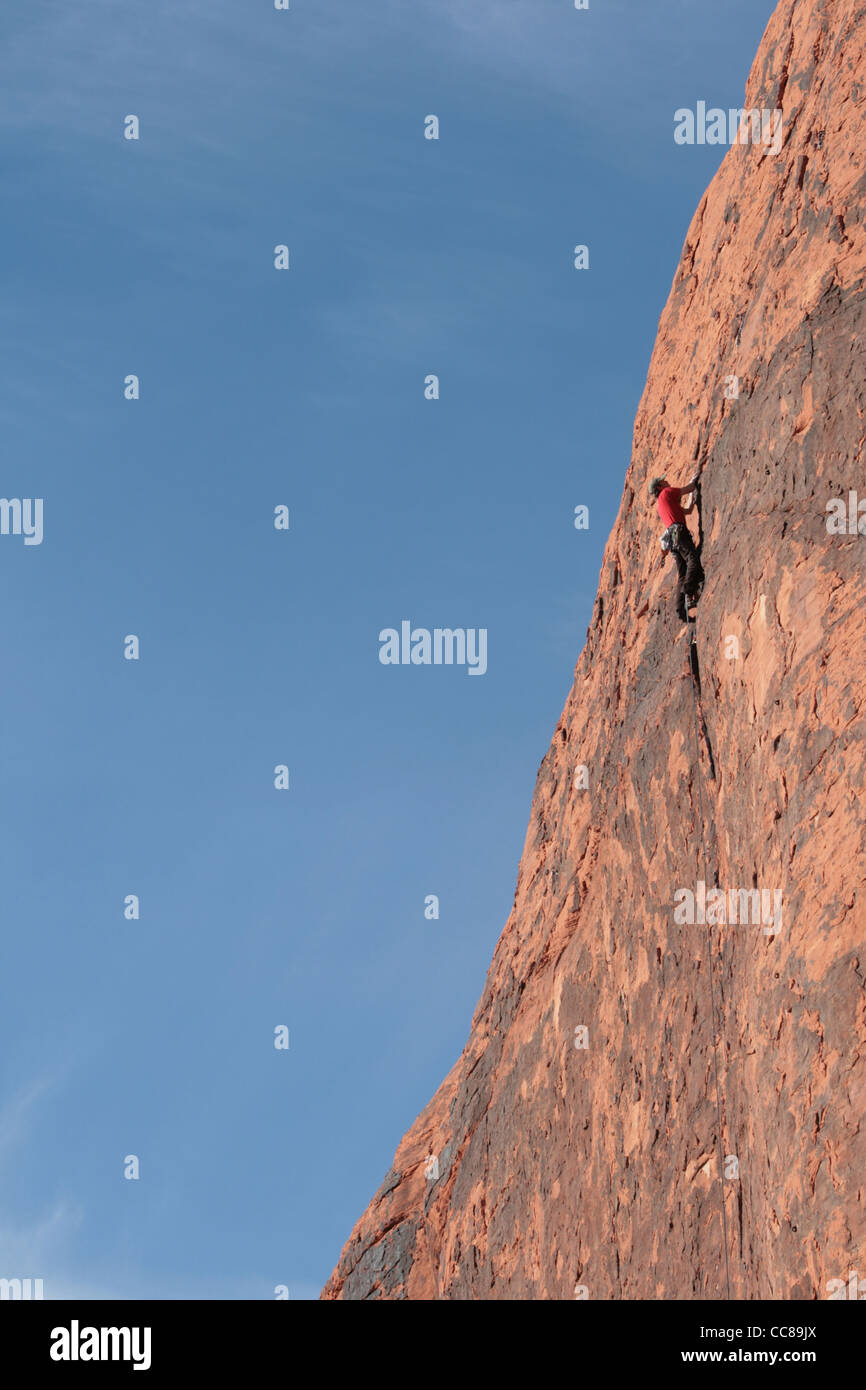 vertical view of a rock climber in red climbing a tall red sandstone ...