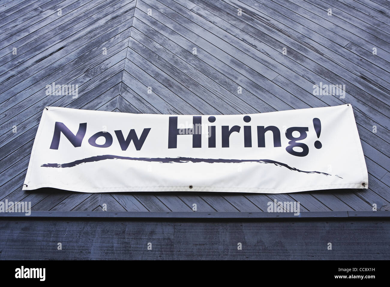 now hiring sign hung on building wall Stock Photo - Alamy