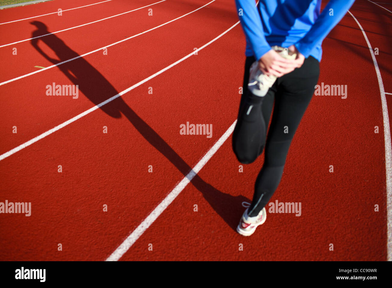 Young woman stretching before her run casts a shadow on the track Stock ...