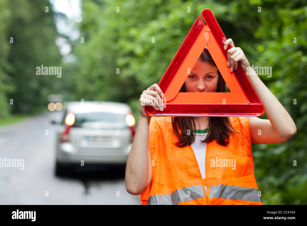 Young female driver wearing a high visibility vest after her car has ...