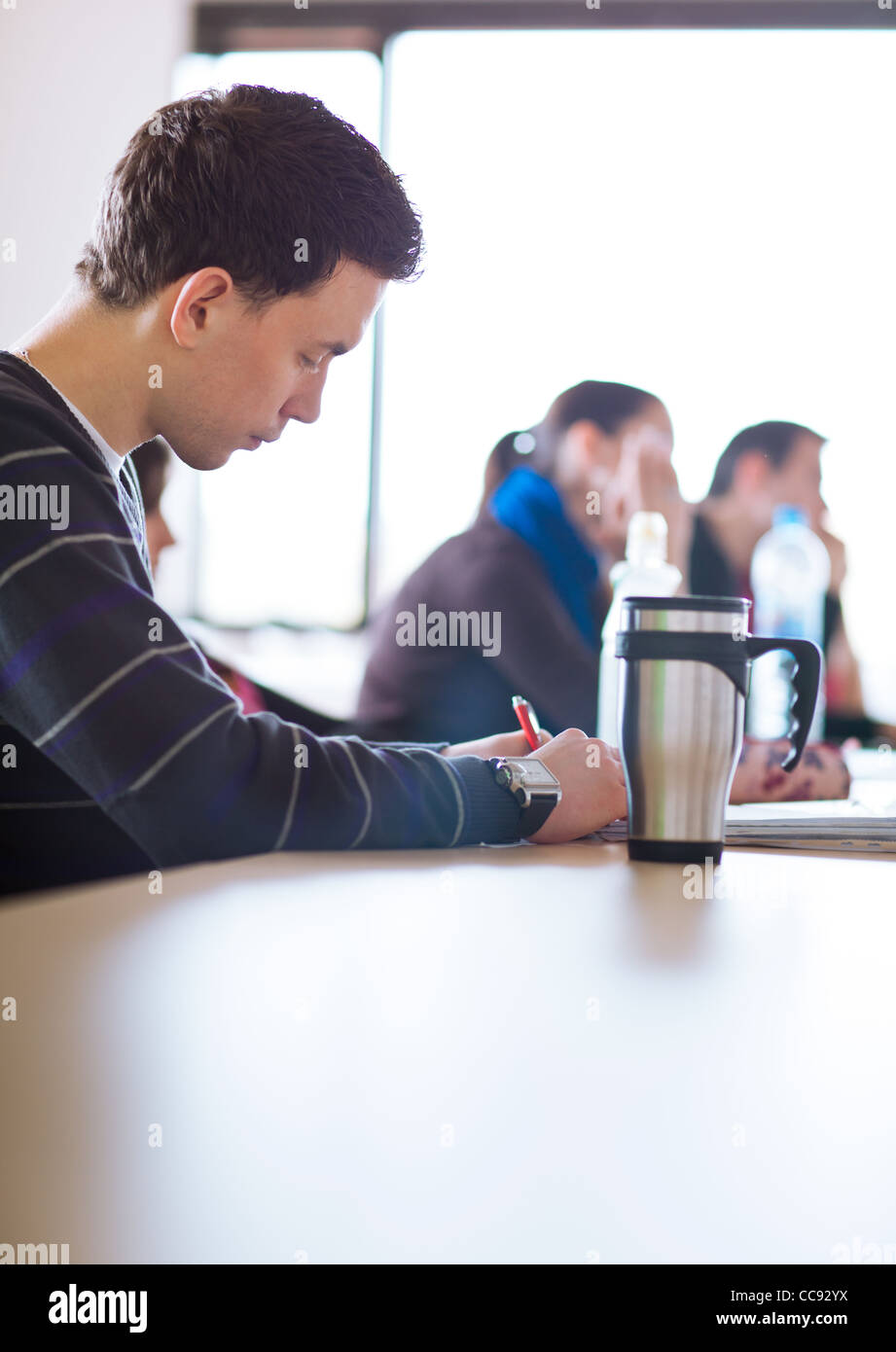 young, handsome male college student sitting in a classroom full of ...