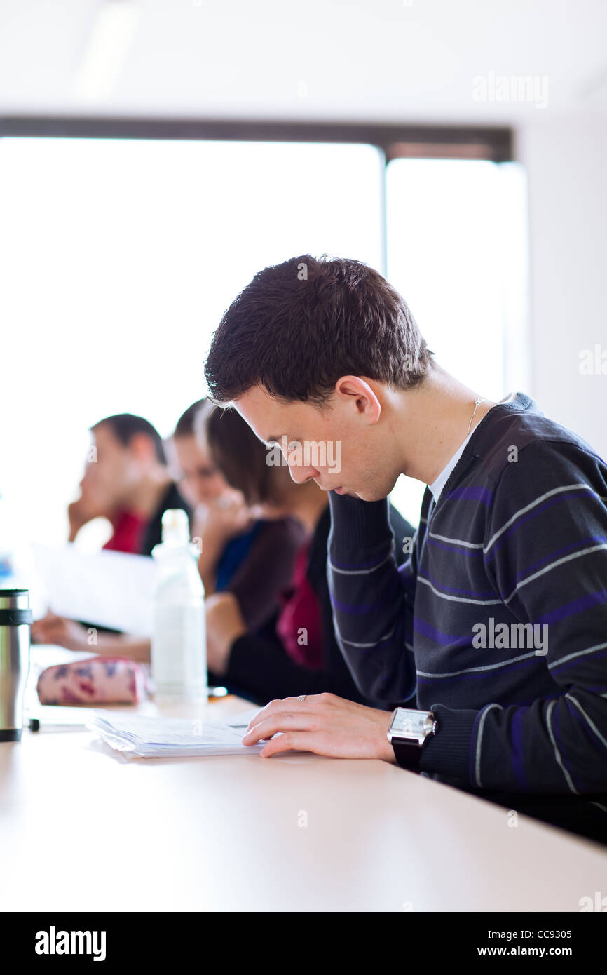 young, handsome male college student sitting in a classroom full of ...