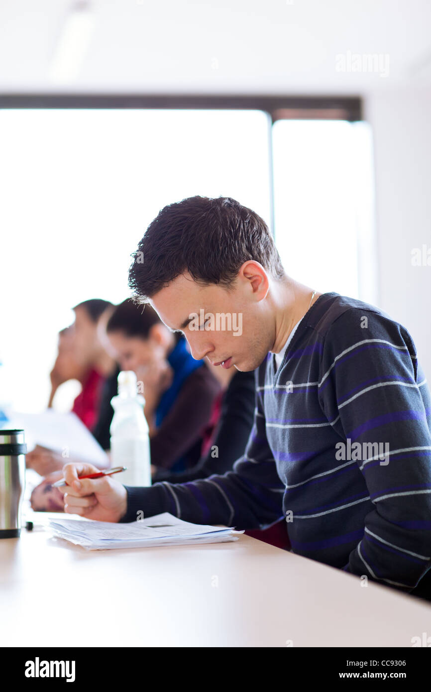 young, handsome male college student sitting in a classroom full of ...