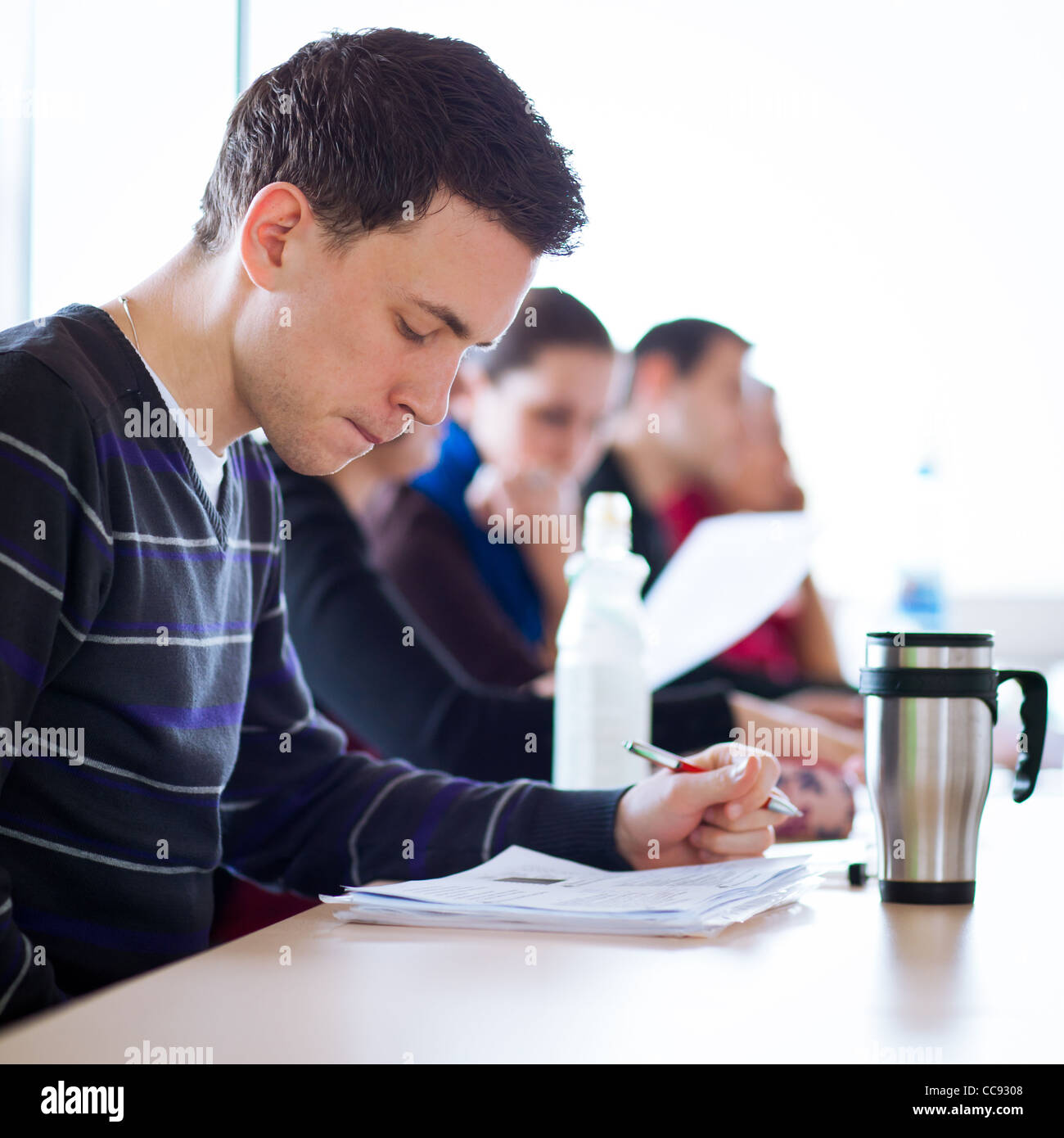 young, handsome male college student sitting in a classroom full of ...
