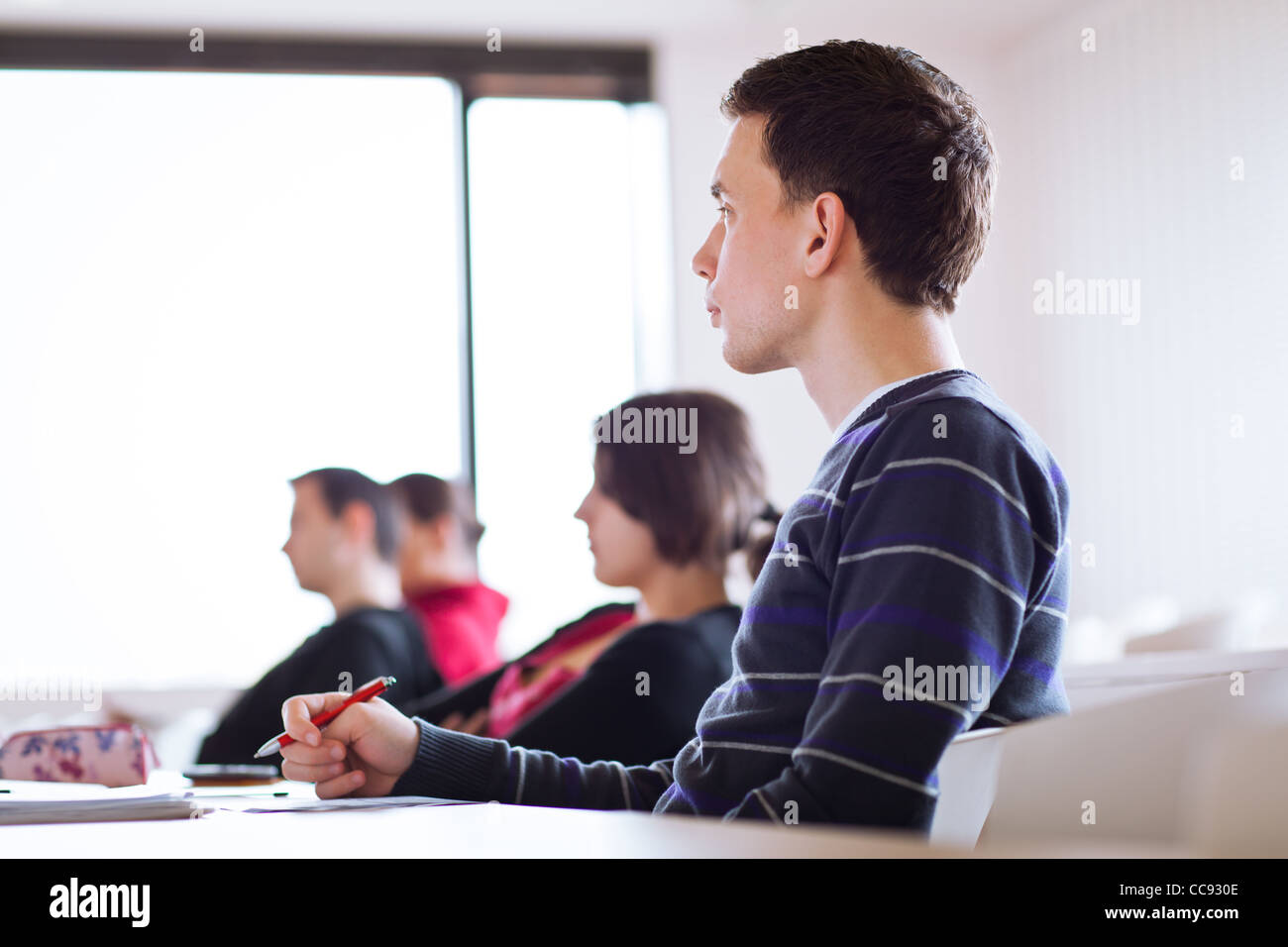 young, handsome male college student sitting in a classroom full of ...