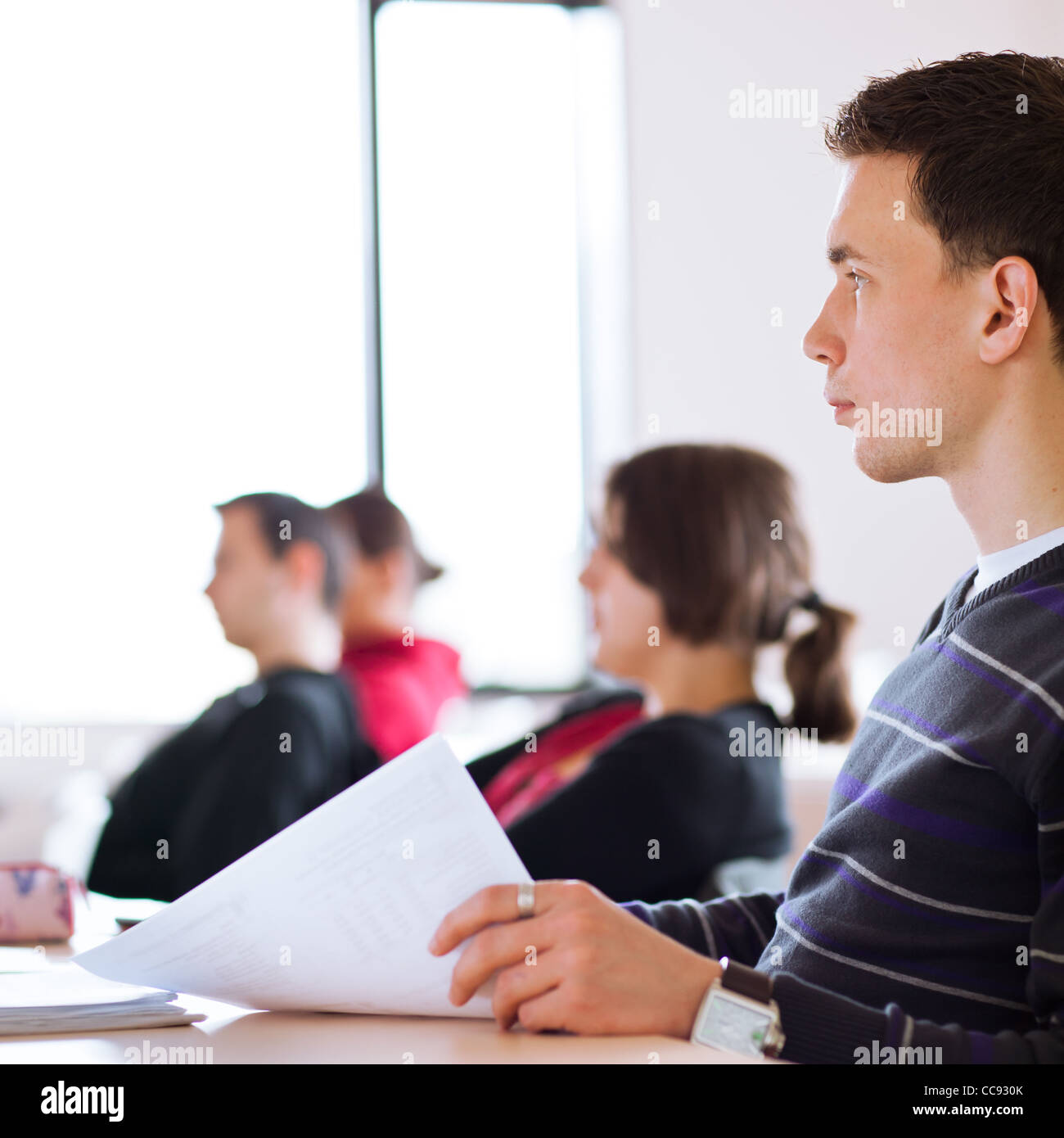young, handsome male college student sitting in a classroom full of ...
