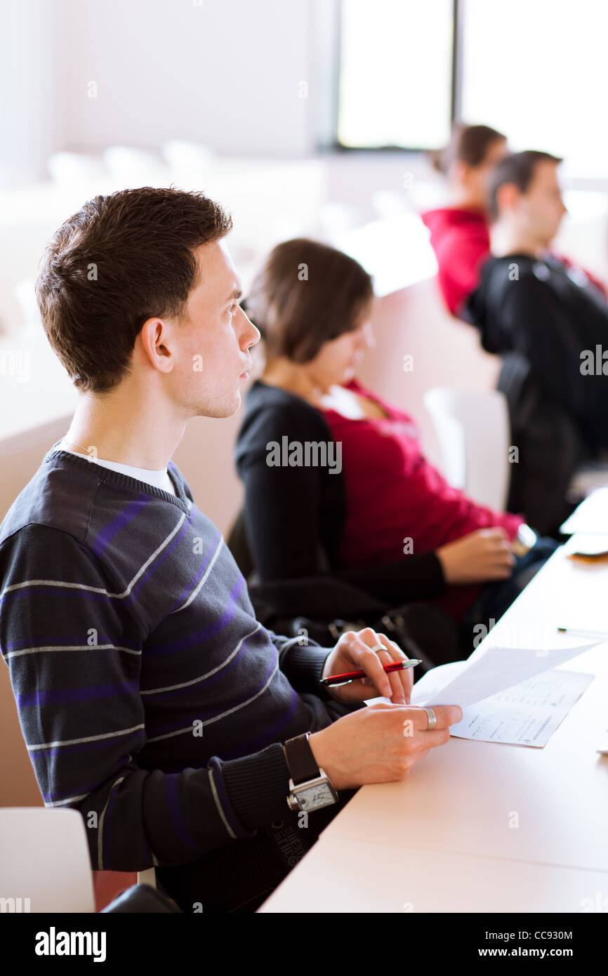 young, handsome male college student sitting in a classroom full of ...