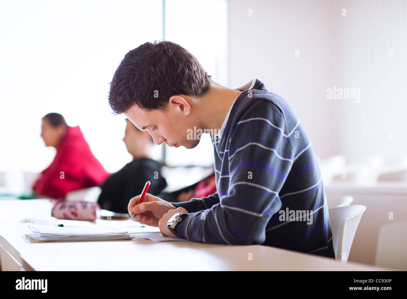 young, handsome male college student sitting in a classroom full of ...