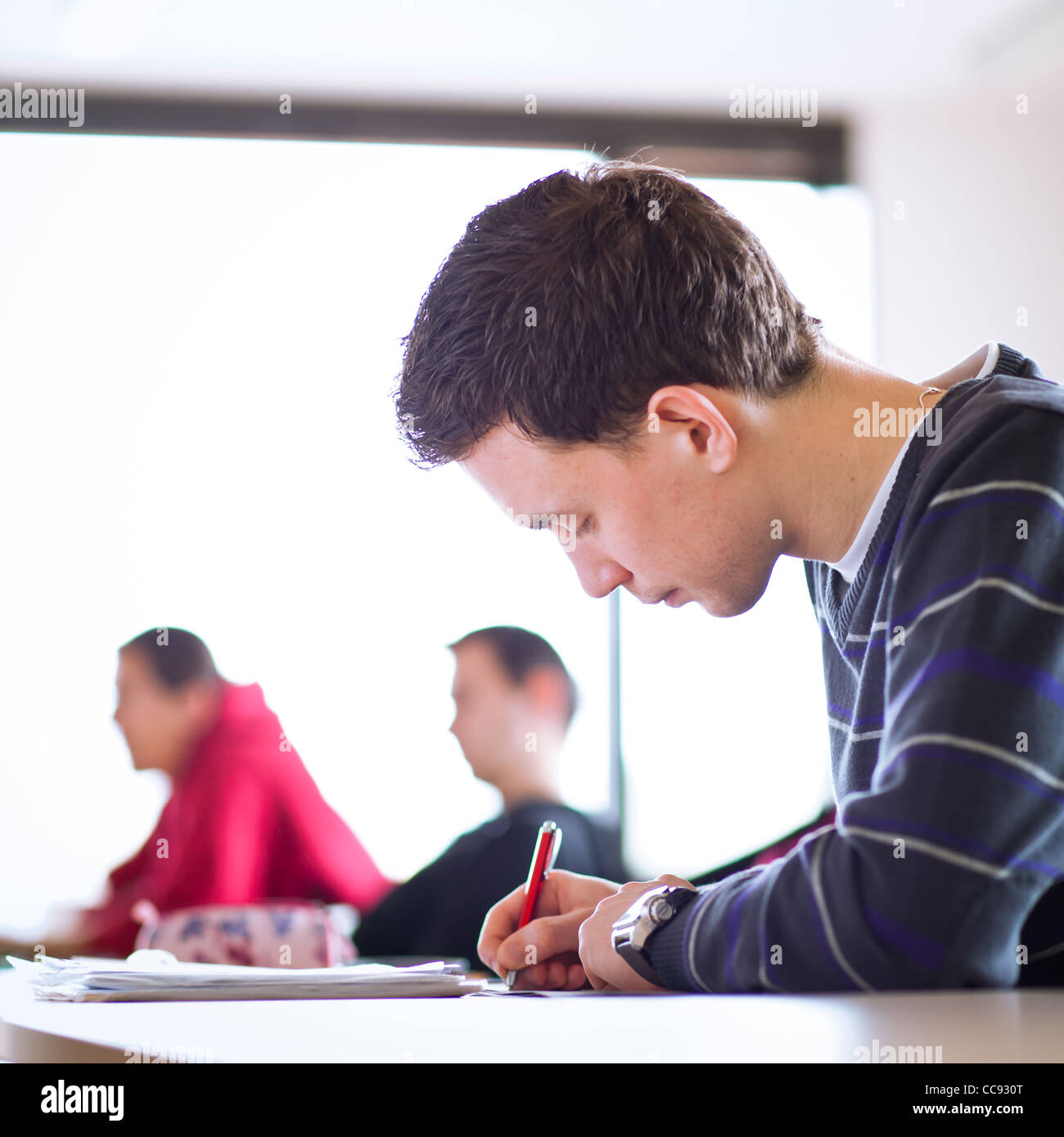 young, handsome male college student sitting in a classroom full of ...