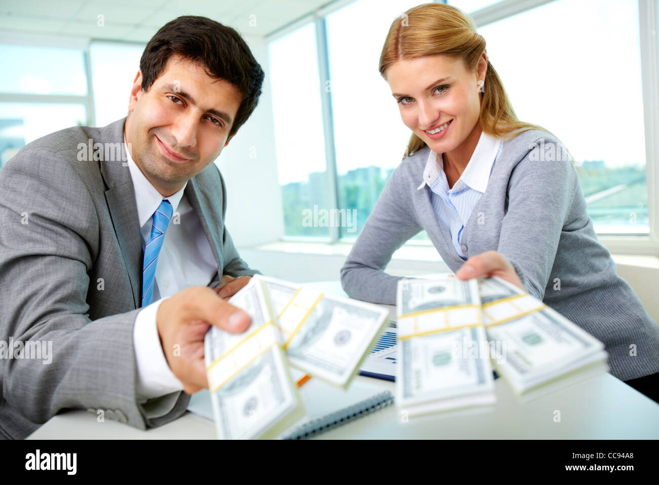 Two business partners at workplace giving money and looking at you ...