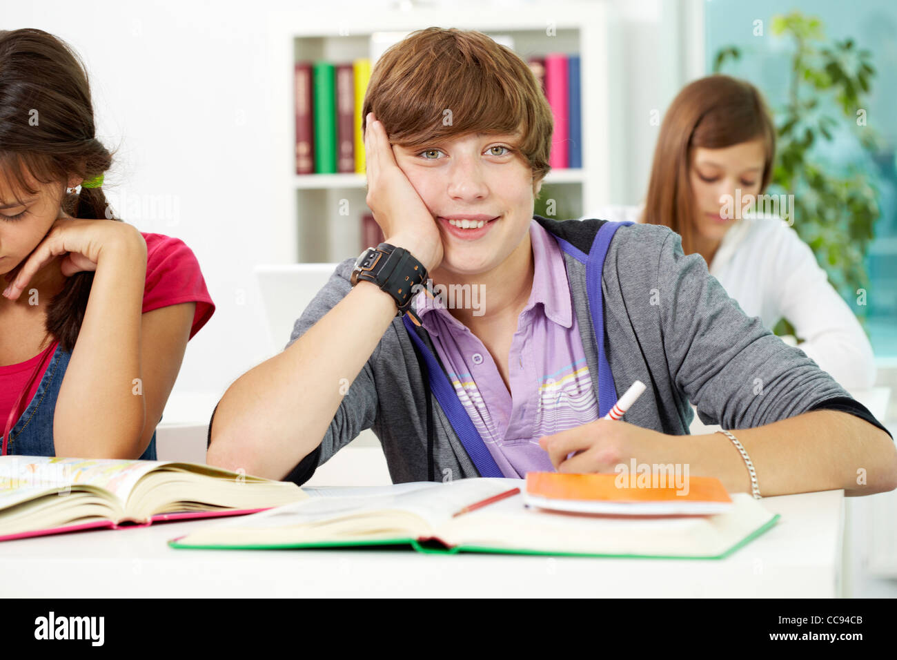 Portrait of smart guy making notes in copybook with his classmate ...