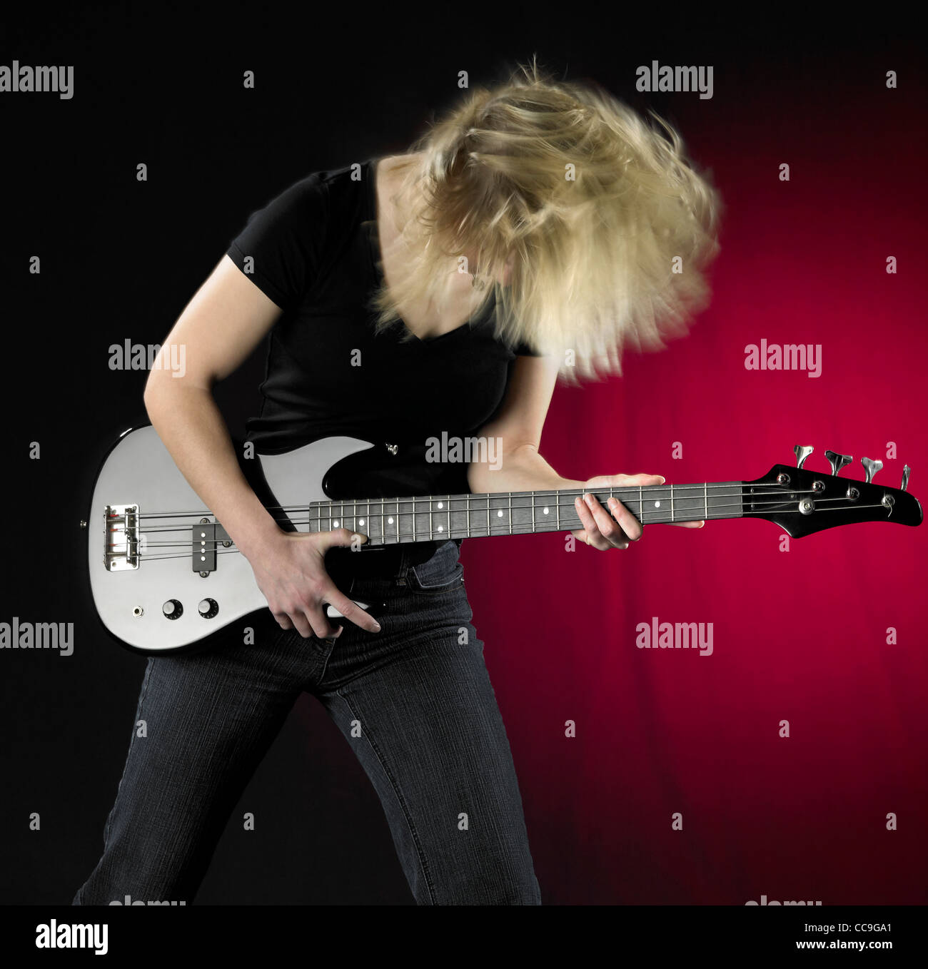 a woman playing a black bass guitar in front of partly reddish back ...