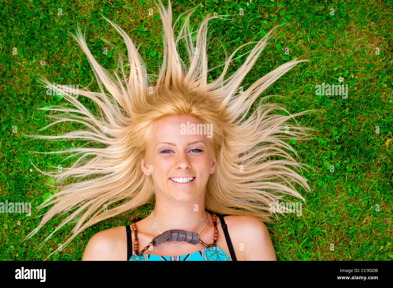 Young woman laying on green grass with hair like a sun around her head ...