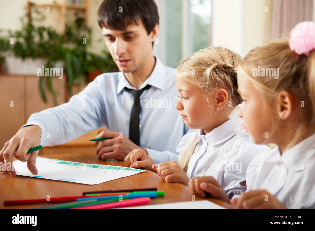 Teacher helping students with schoolwork in school classroom ...