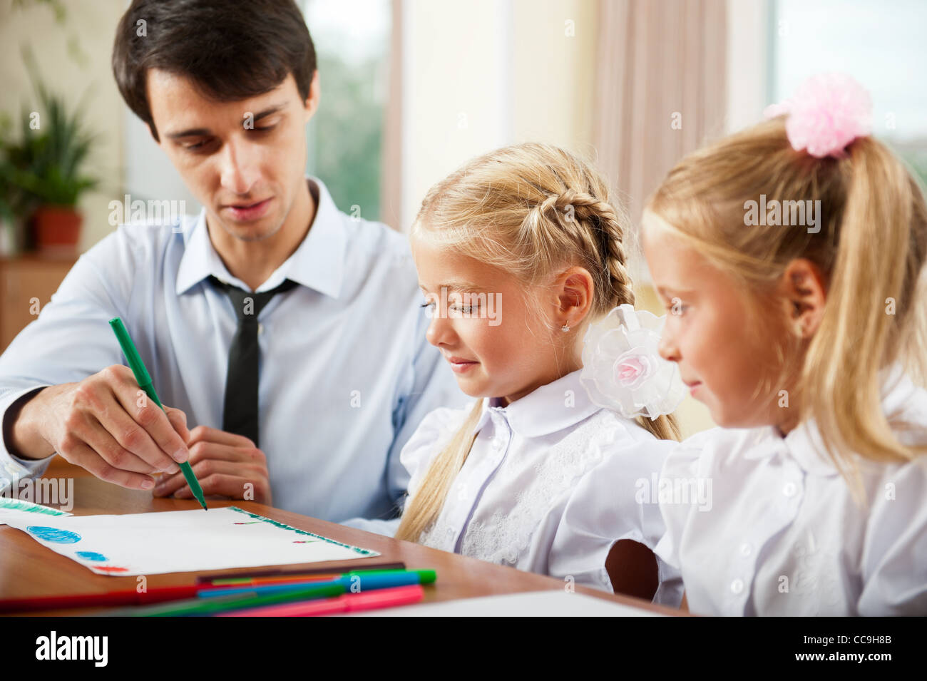 Teacher helping students with schoolwork in school classroom ...