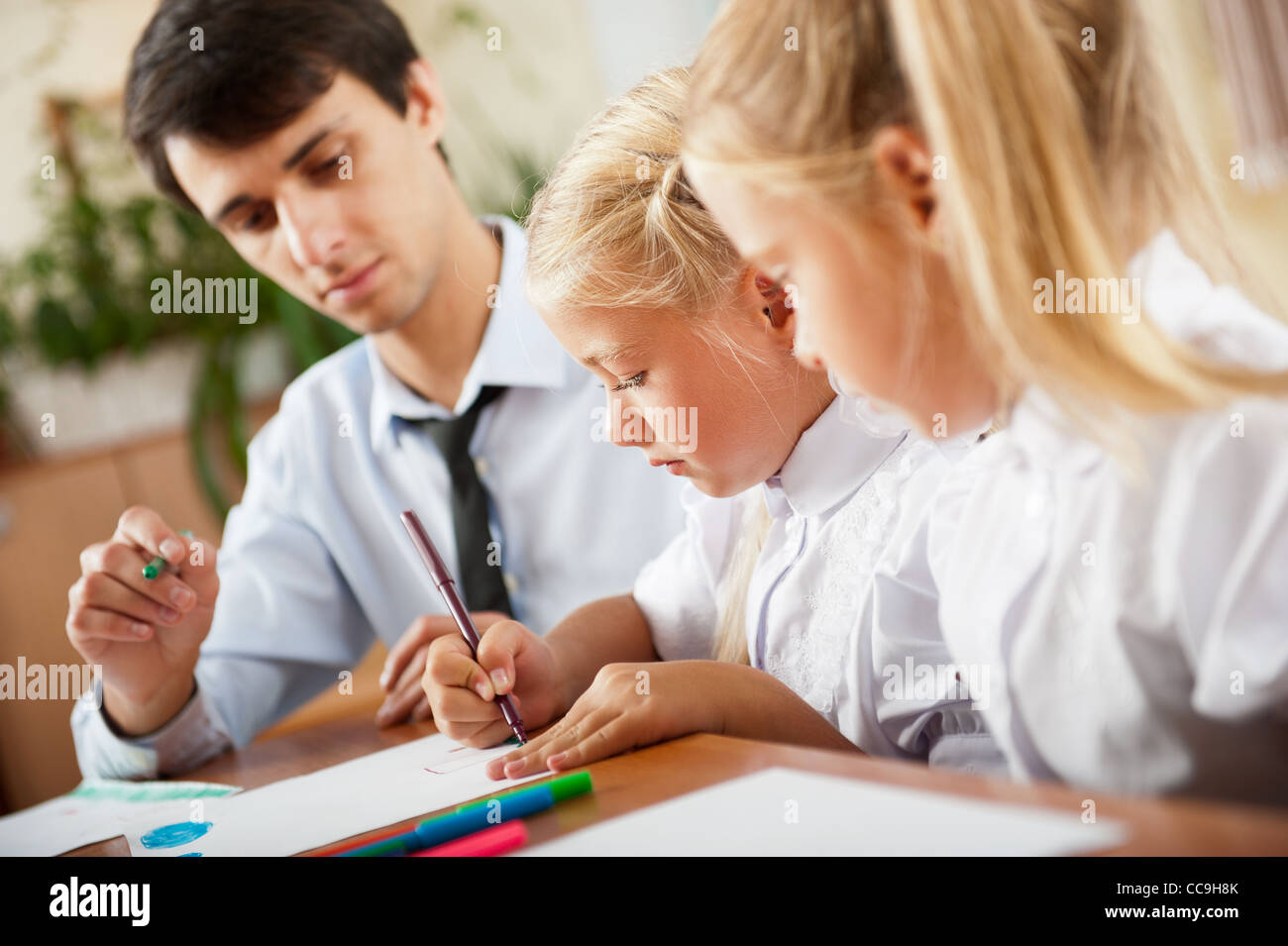 Teacher helping students with schoolwork in school classroom ...