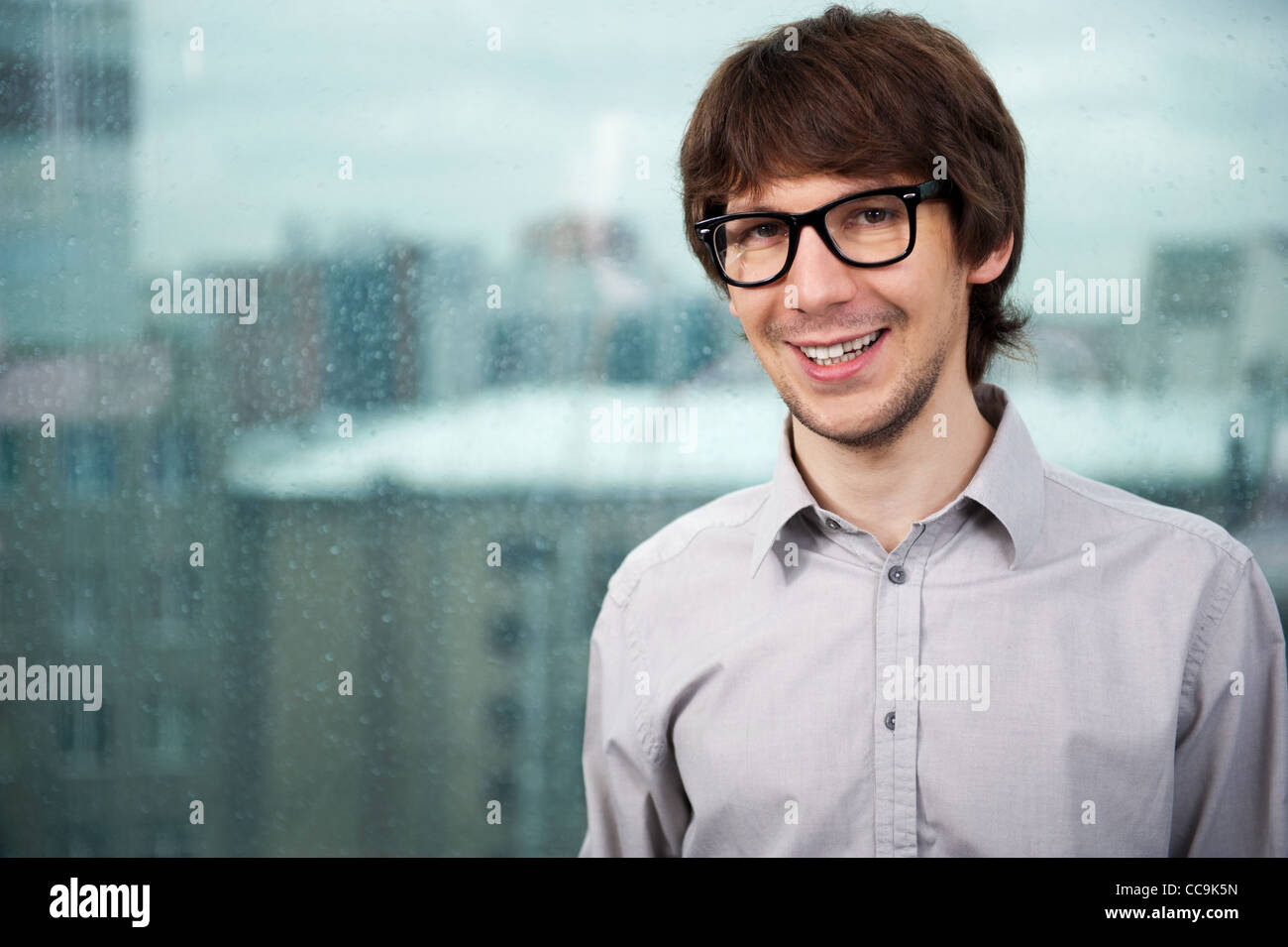 Closeup of a young smiling business man standing against big window ...