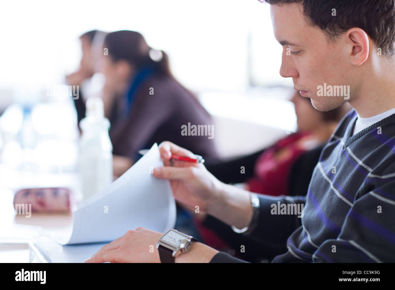 young, handsome male college student sitting in a classroom full of ...