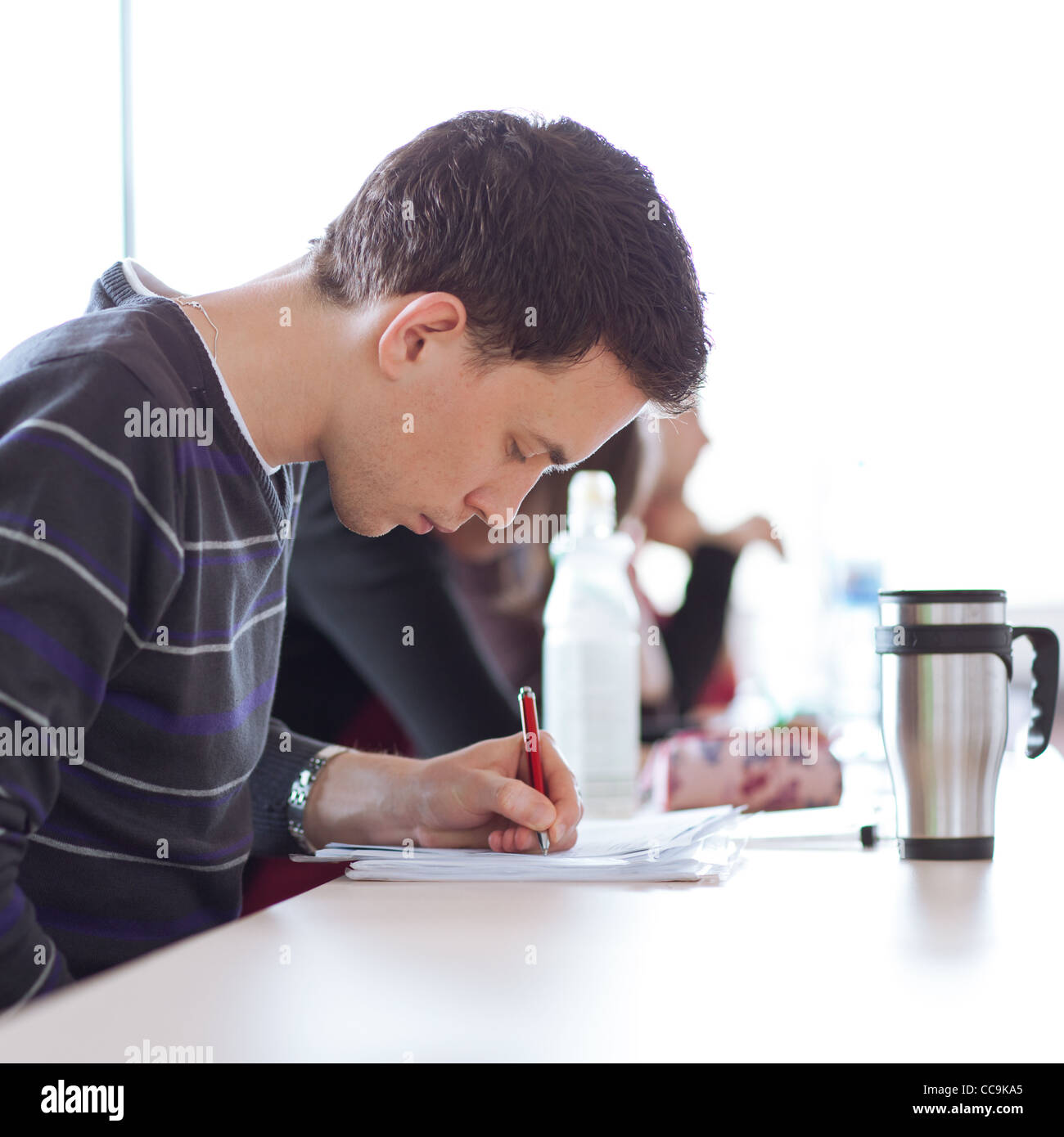 young, handsome male college student sitting in a classroom full of ...