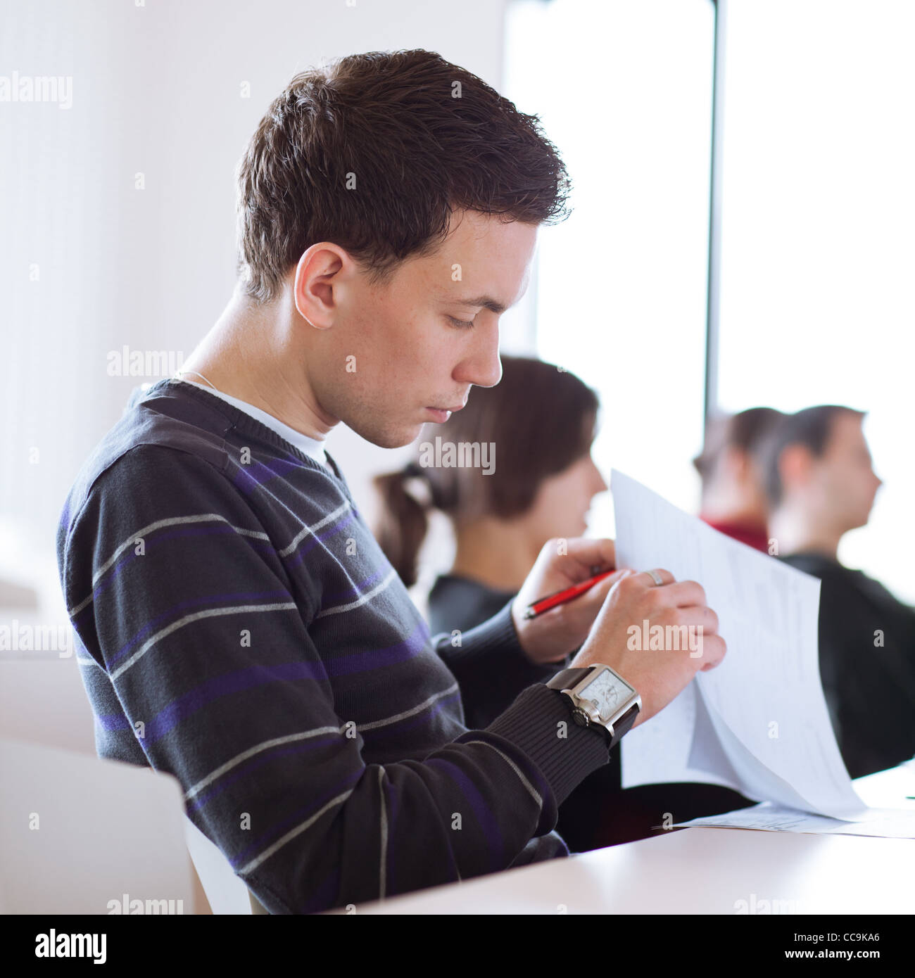 young, handsome male college student sitting in a classroom full of ...