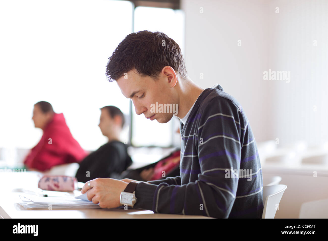 young, handsome male college student sitting in a classroom full of ...