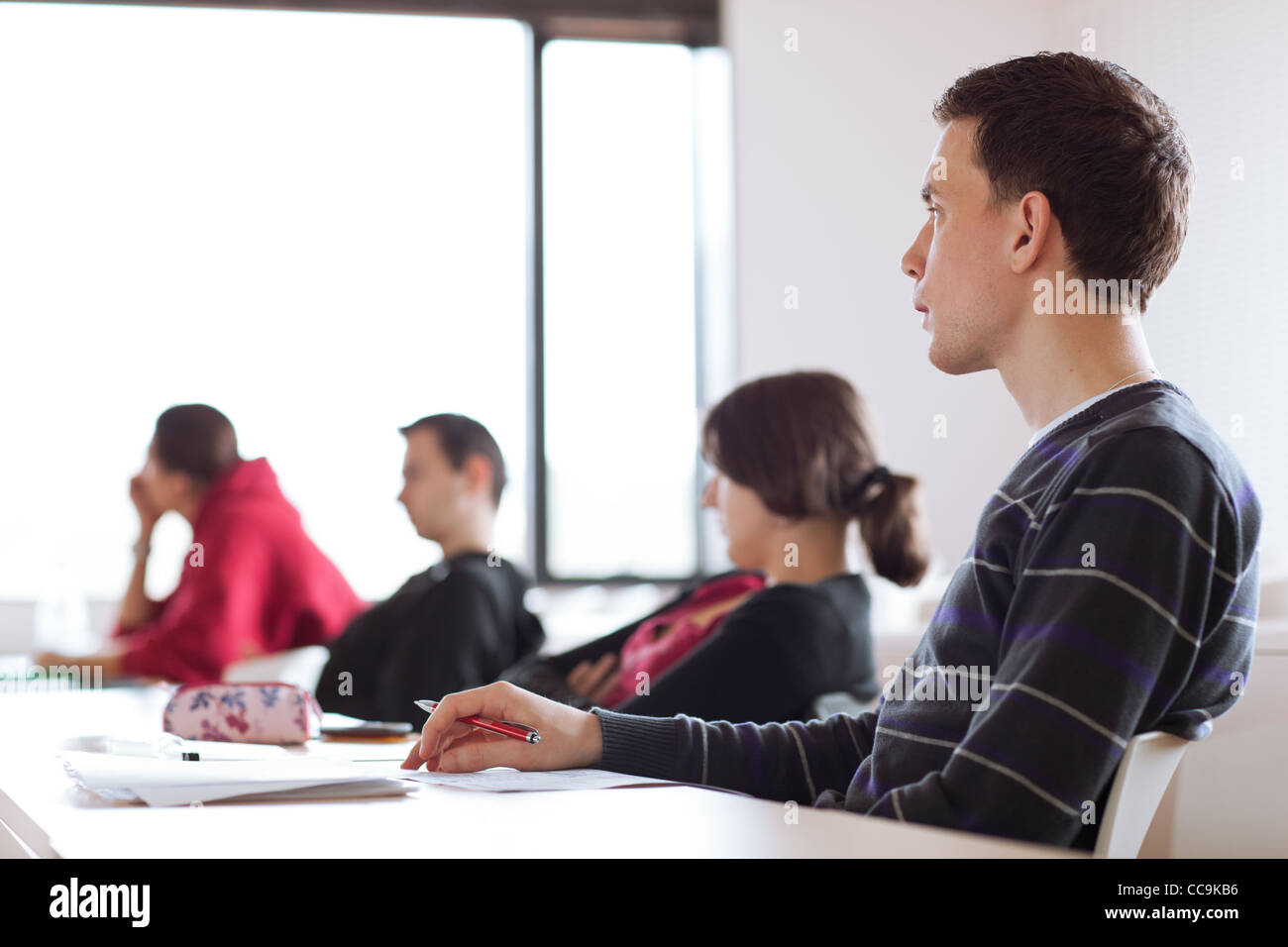 young, handsome male college student sitting in a classroom full of ...