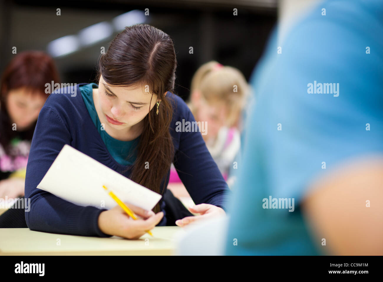 pretty female college student sitting in a classroom full of students ...