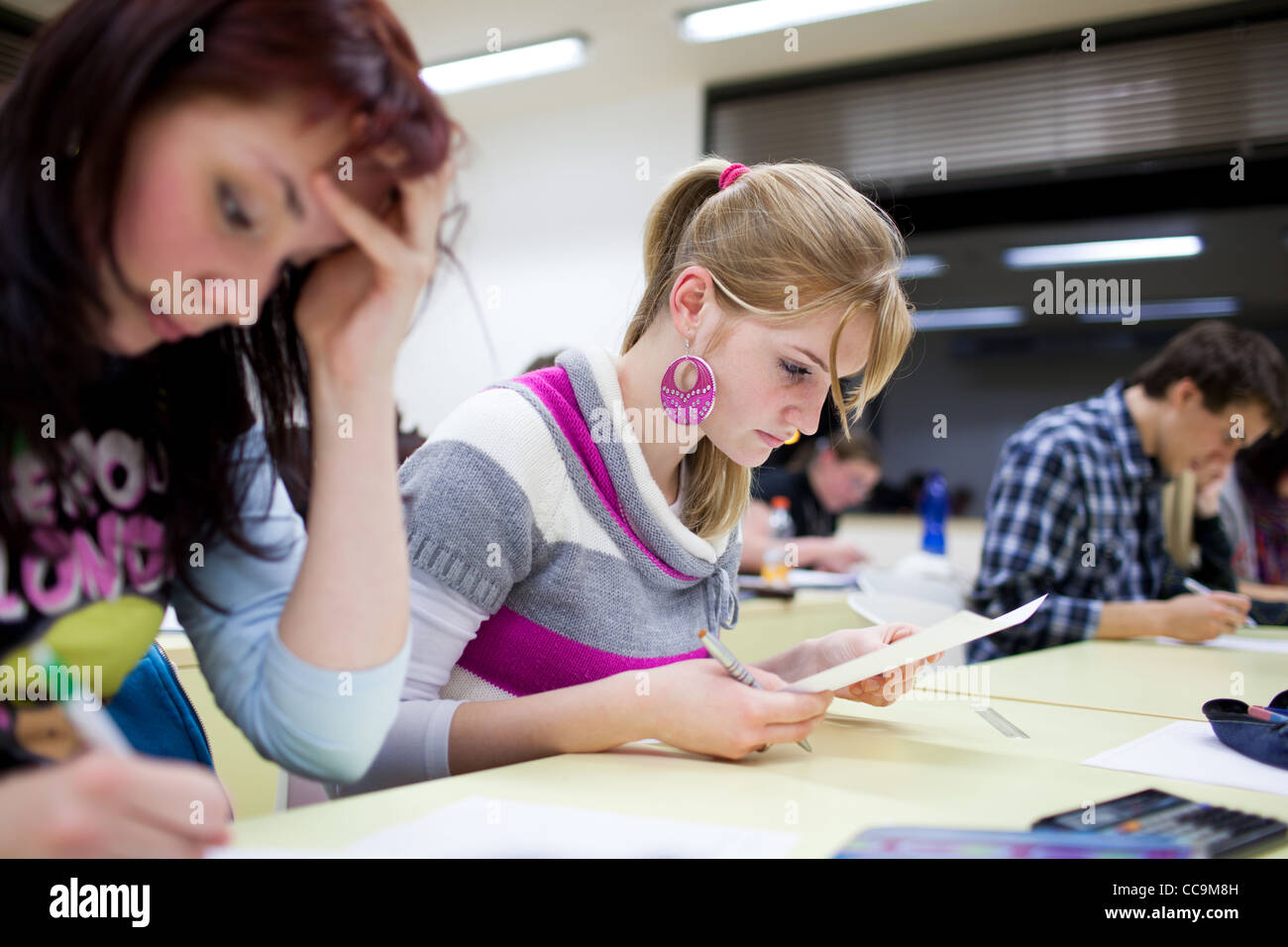 pretty female college student sitting in a classroom full of students ...