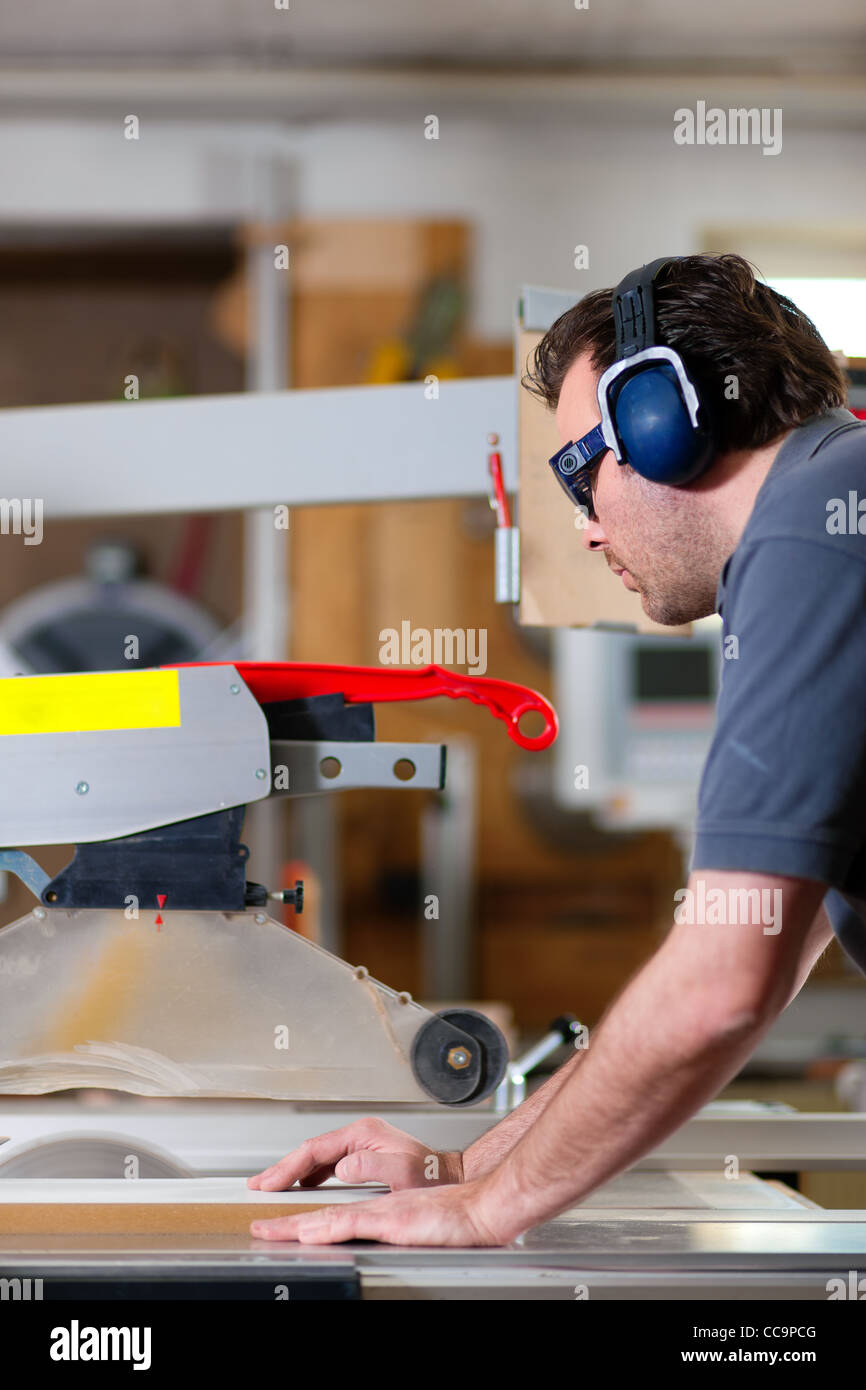 Carpenter working on an electric buzz saw cutting some boards, he is ...