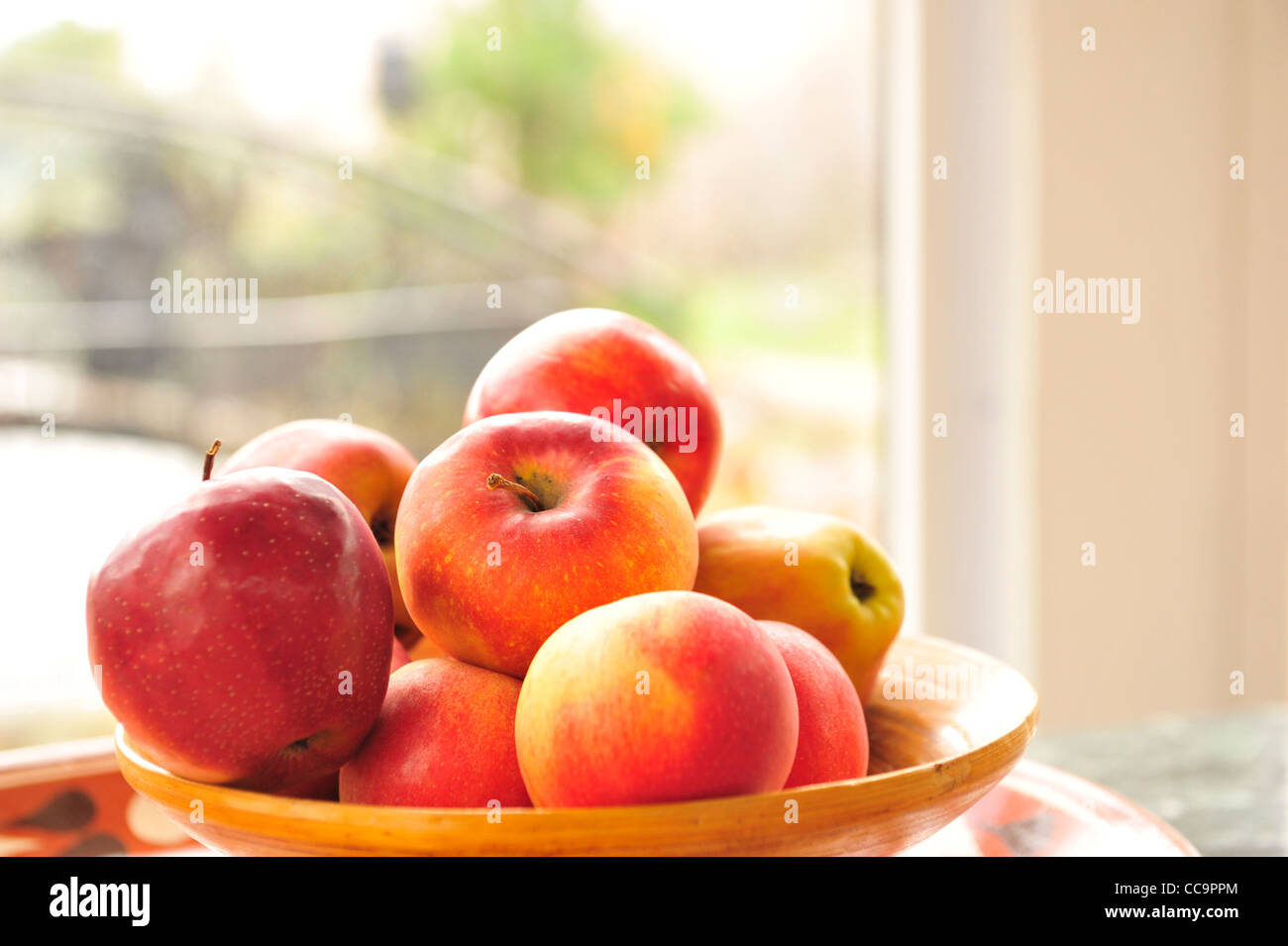 Closeup photo of red apples on wooden plate indoor against wide window ...