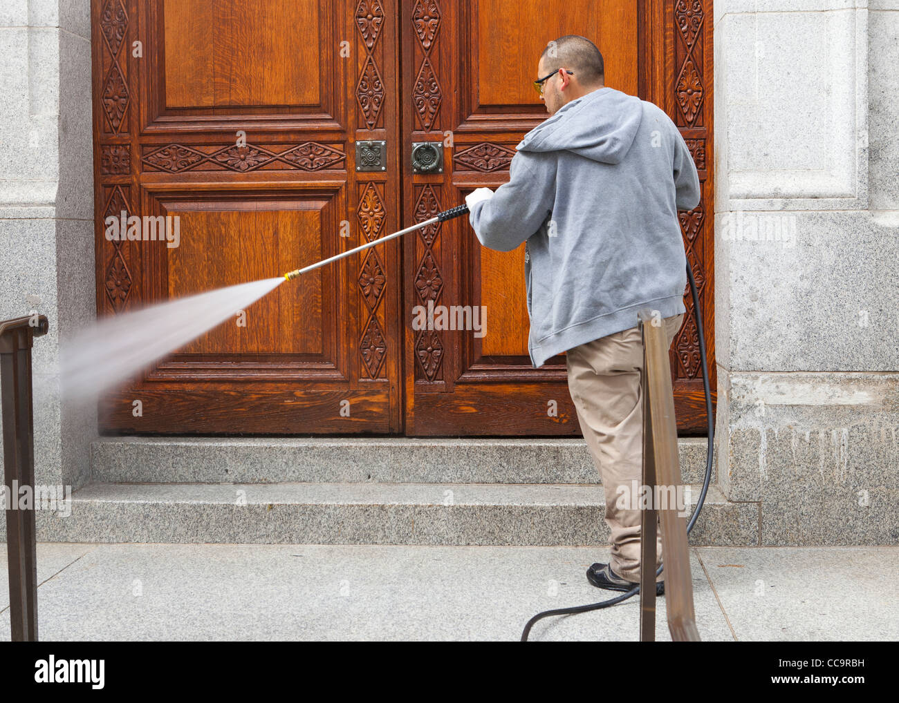 A maintenance man cleaning entrance of building using a pressure washer ...