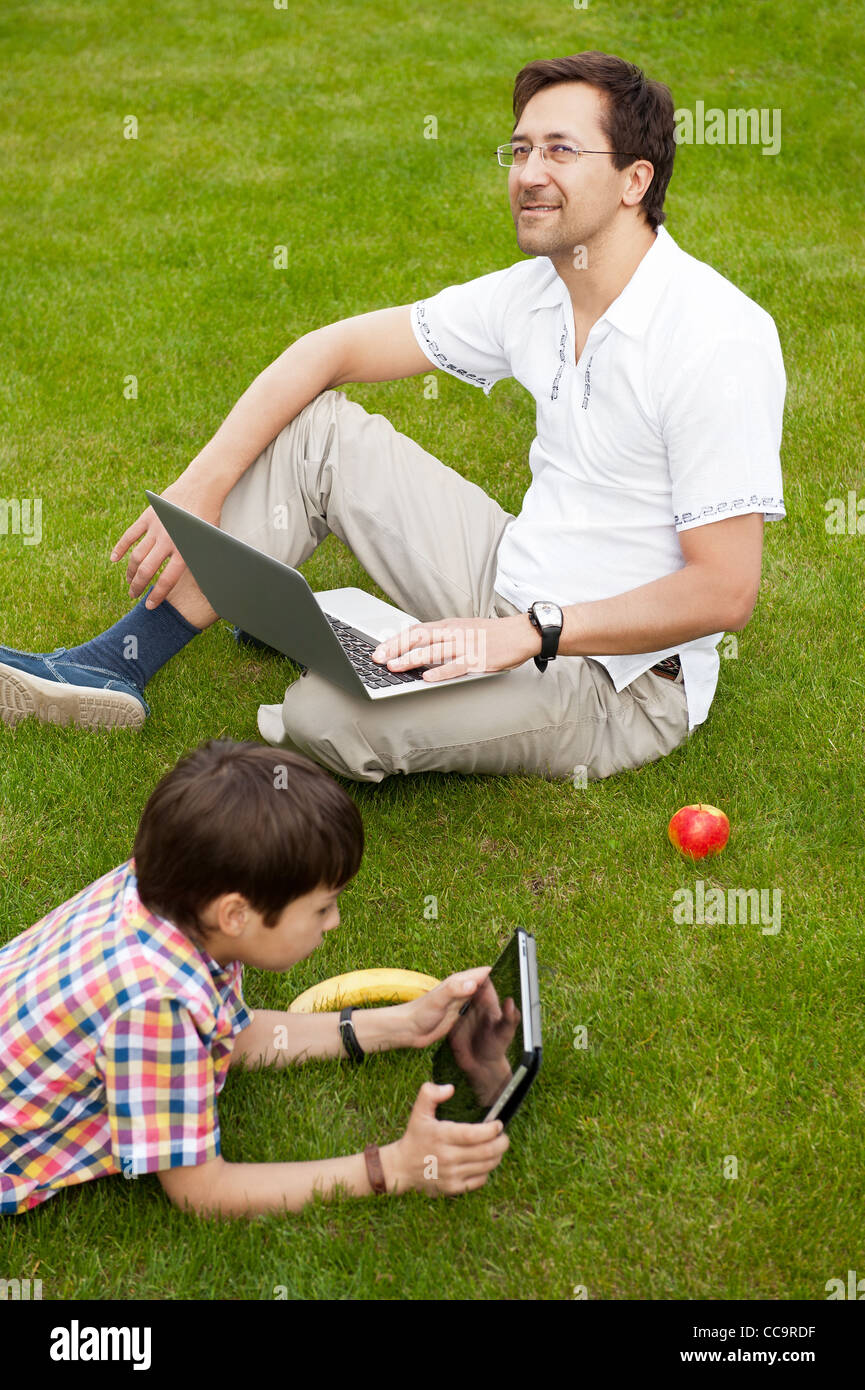 Man and young boy his son sitting outdoors on their backyard using ...