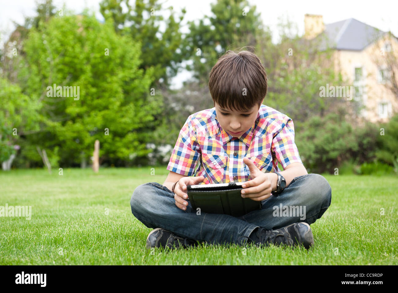 Young boy outdoors on the grass at backyard using his tablet computer ...