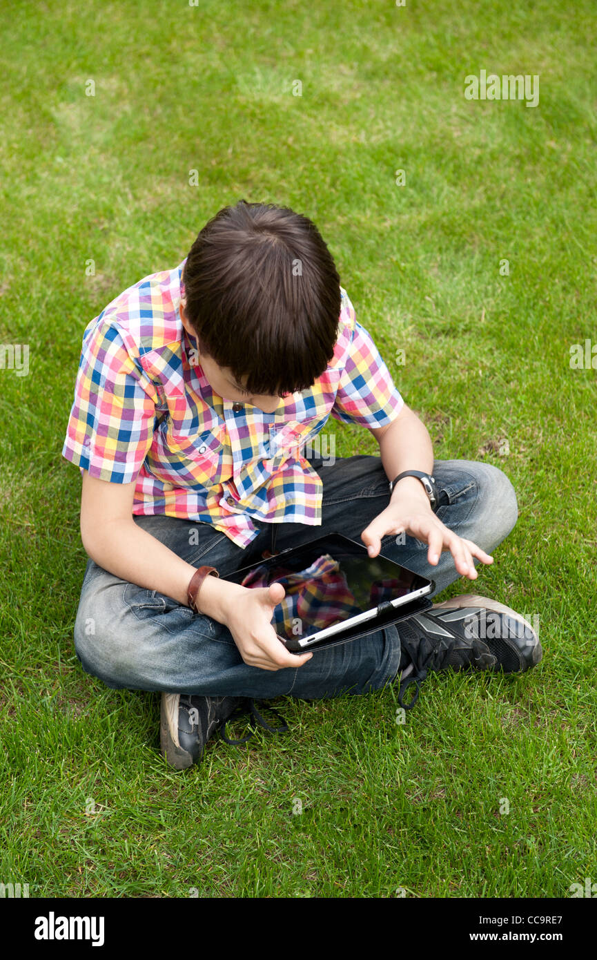 Young boy outdoors on the grass at backyard using his tablet computer ...