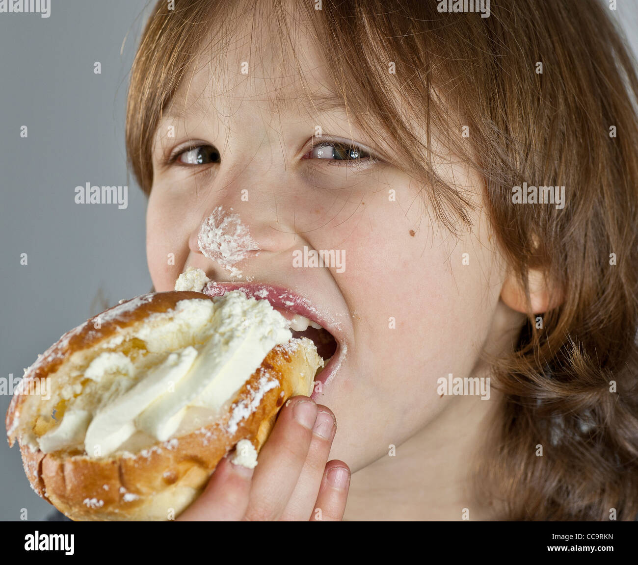 Boy enjoying a cream bun with almond paste getting cream on his noose ...