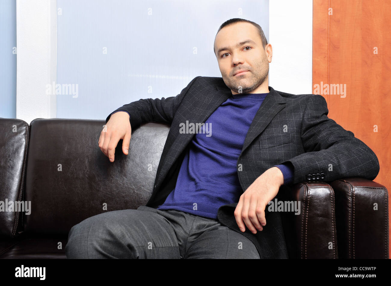 Handsome smiling man seating on the sofa Stock Photo - Alamy