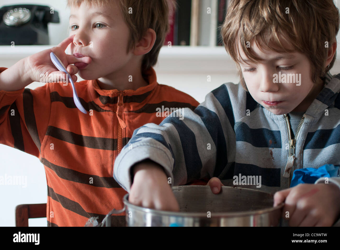 Two young boys baking a chocolate cake - licking the cake mixture out ...