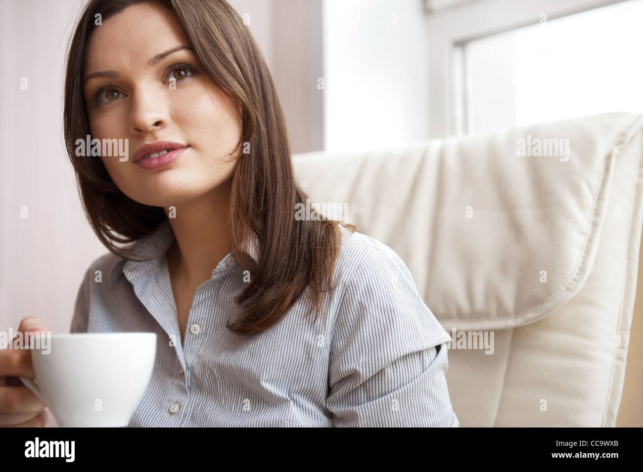 Young woman at home sipping tea from a cup sitting on comfortable ...