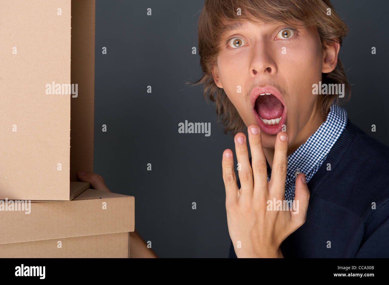 Portrait of young man with boxes against grey wall. He is afraid of ...