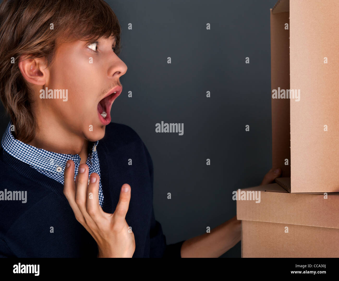 Portrait of young man with boxes against grey wall. He is afraid of ...